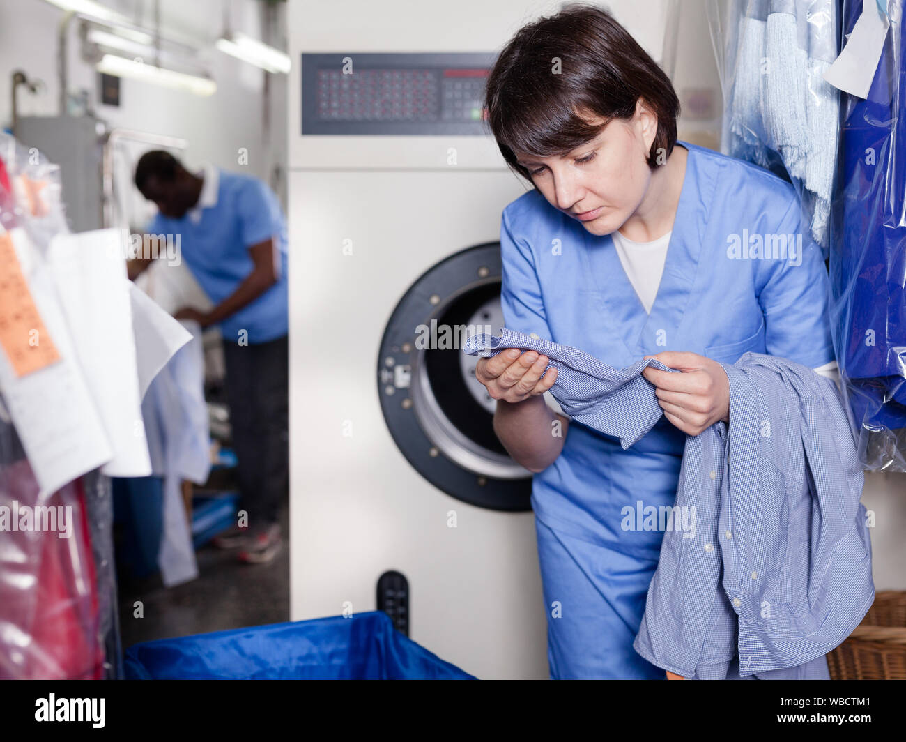 Focused female laundry worker sorting dirty clothes before dry cleaning ...