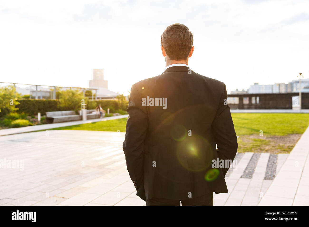 Back view of a young businessman wearing suit standing outdoors at the ...