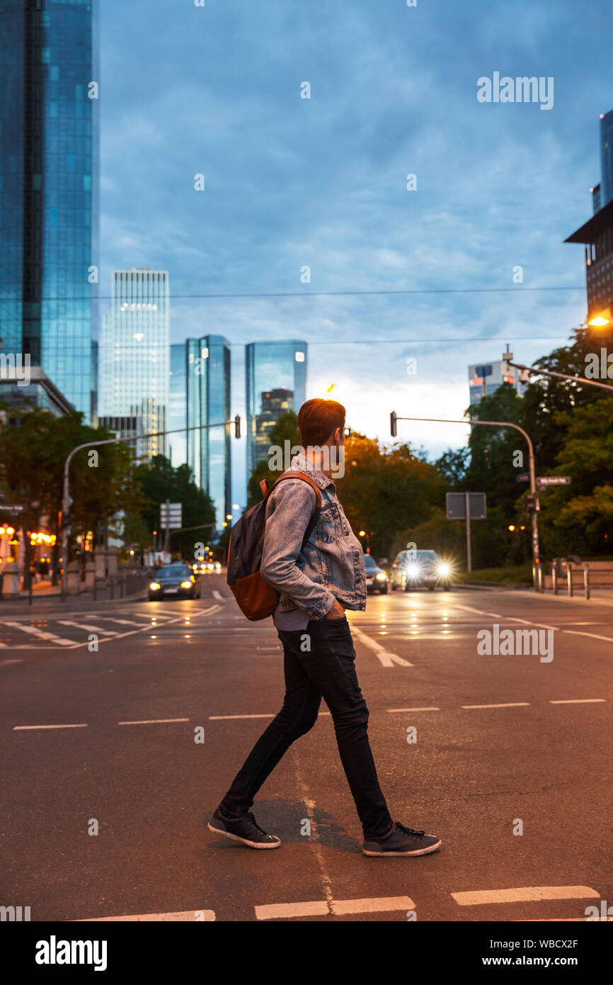 Side view of an attractive young man walking at the city streets in the ...