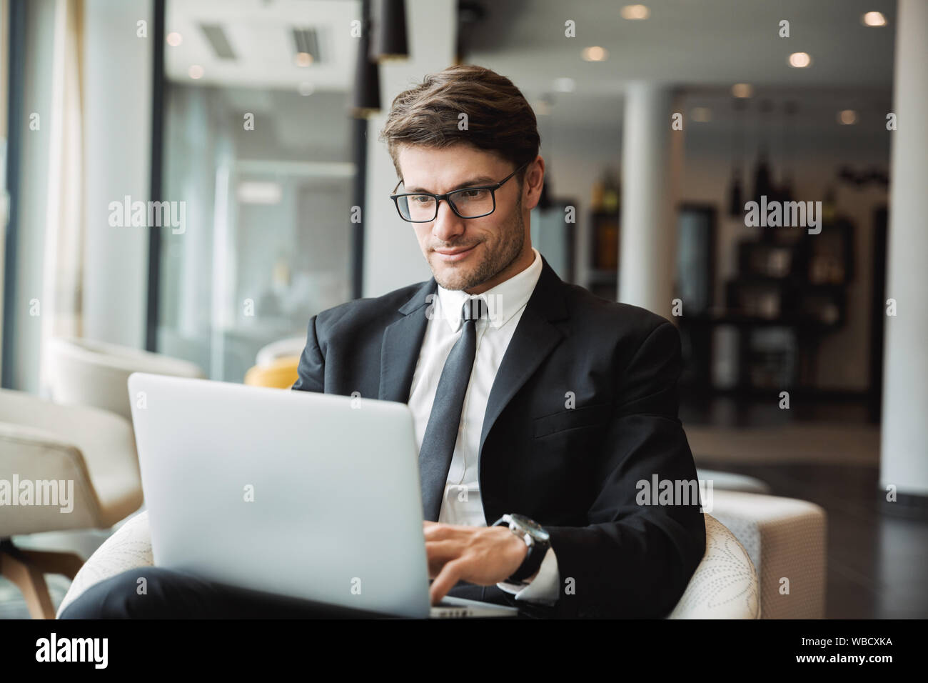 Portrait of pleased young businessman wearing formal black suit sitting ...