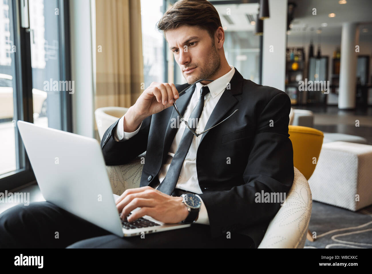 Portrait of serious young businessman wearing formal black suit sitting ...