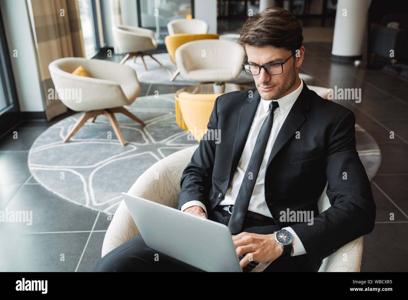 Portrait of stylish young businessman wearing formal black suit sitting ...