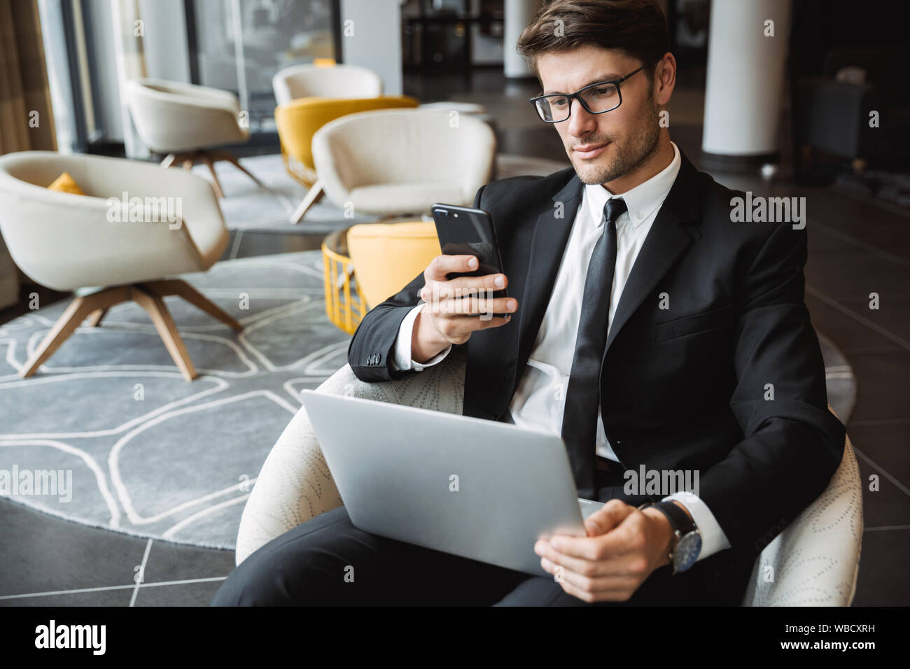 Portrait of handsome businessman wearing formal black suit using laptop ...