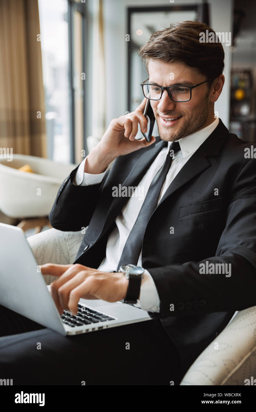 Photo of pleased businessman wearing formal black suit using laptop ...