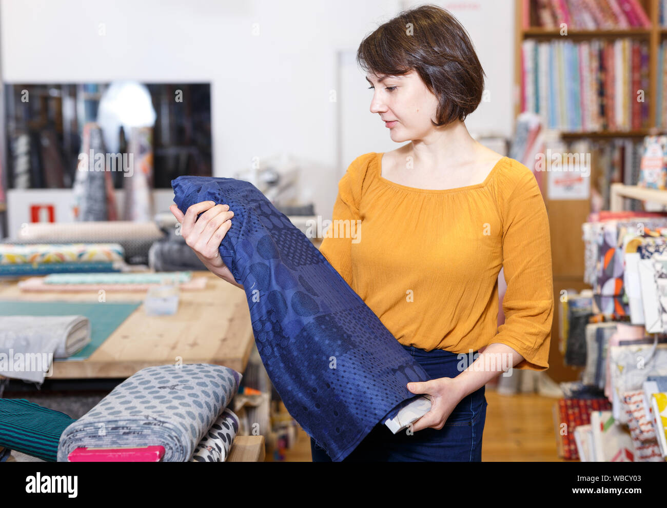 Pensive woman choosing textiles for dressmaking in fabric shop Stock ...