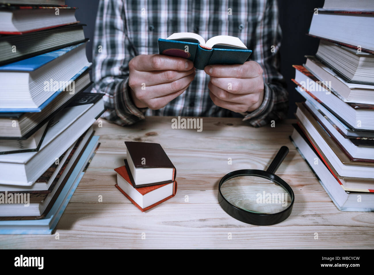 A man reading a miniature book among the big books in the library Stock ...