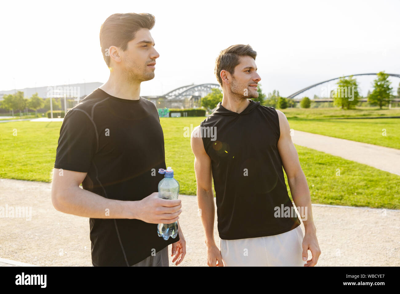 Image of two muscular guys in sportswear drinking water while working ...