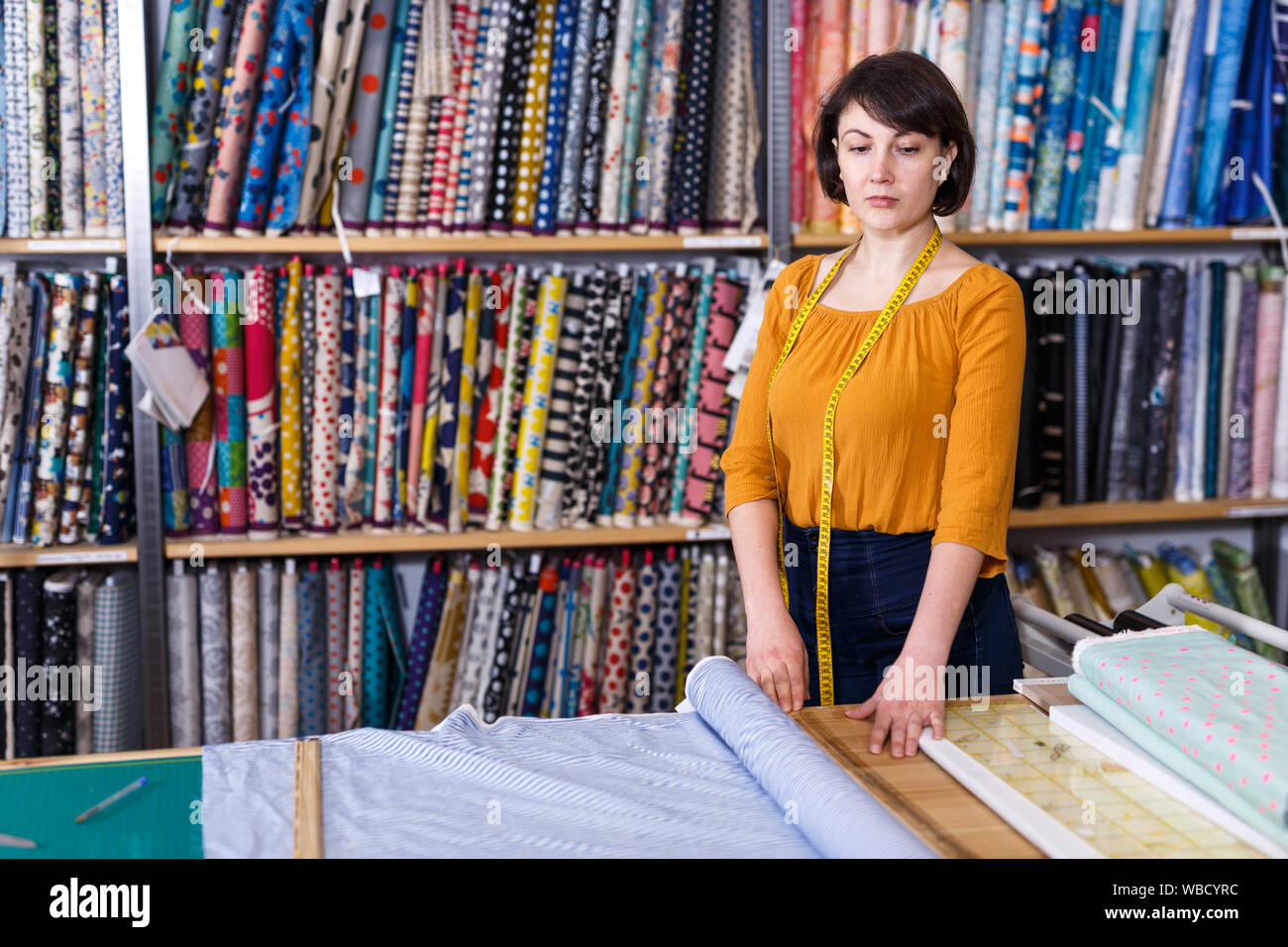 Successful female owner of fabric store standing on background with ...
