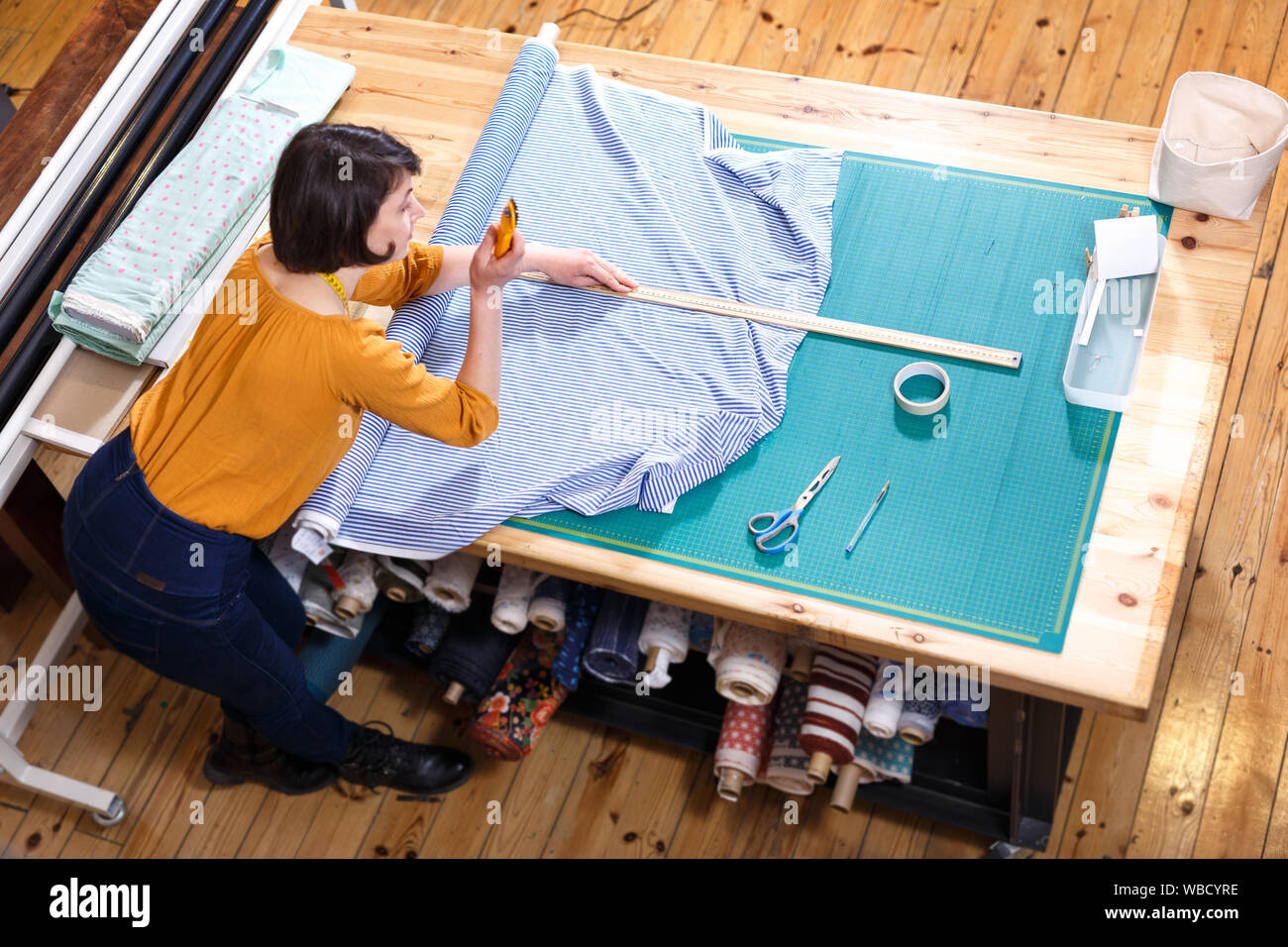 Saleswoman working in fabric store, measuring and cutting off piece of ...