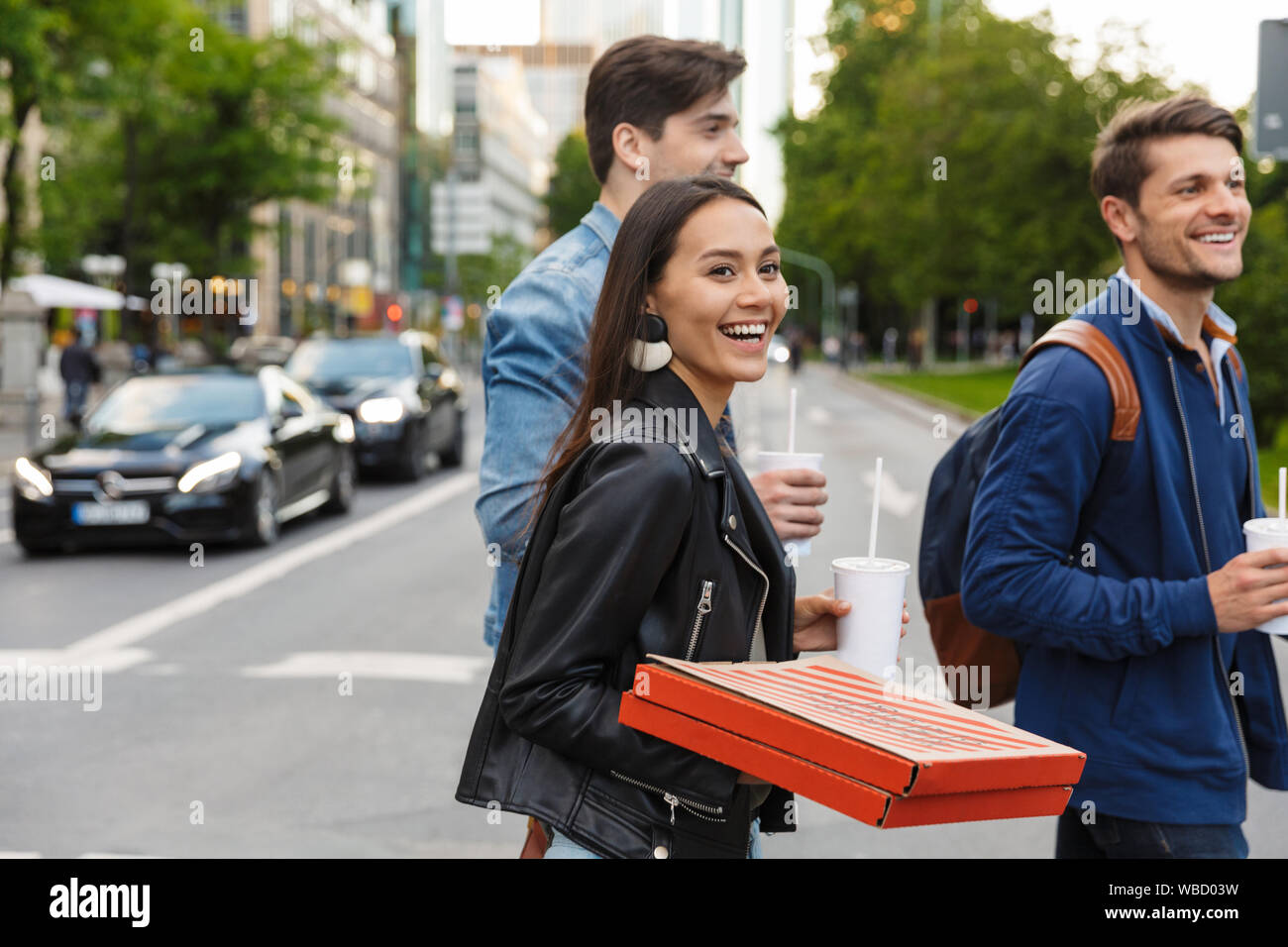 Group of cheerful young friends walking at the city streets, holding ...