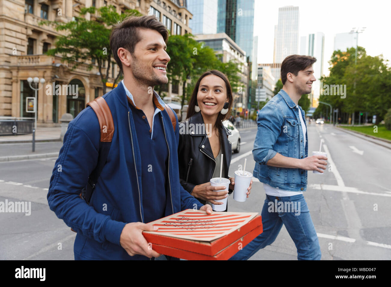 Group of cheerful young friends walking at the city streets, holding ...