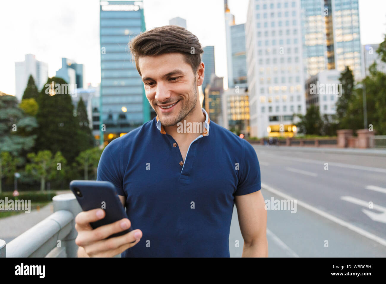 Image of cheerful pleased young man walking outdoors by street in city ...