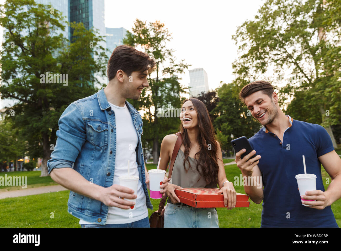 Group of cheerful young friends walking at the city park, holding pizza ...