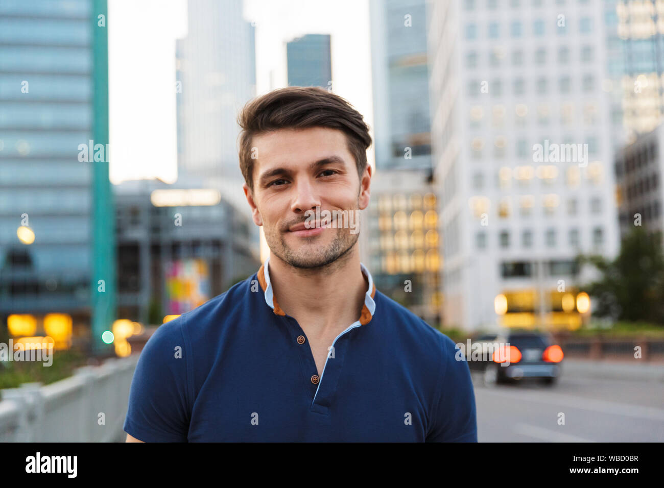Image of smiling cheerful young man walking outdoors by street in city ...