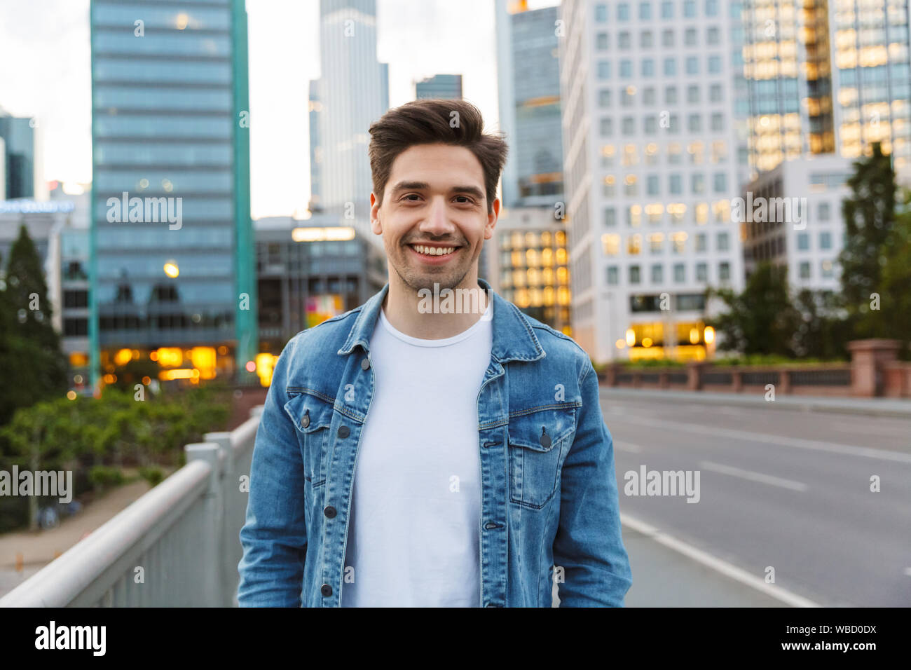 Image of smiling cheerful young man walking outdoors by street in city ...