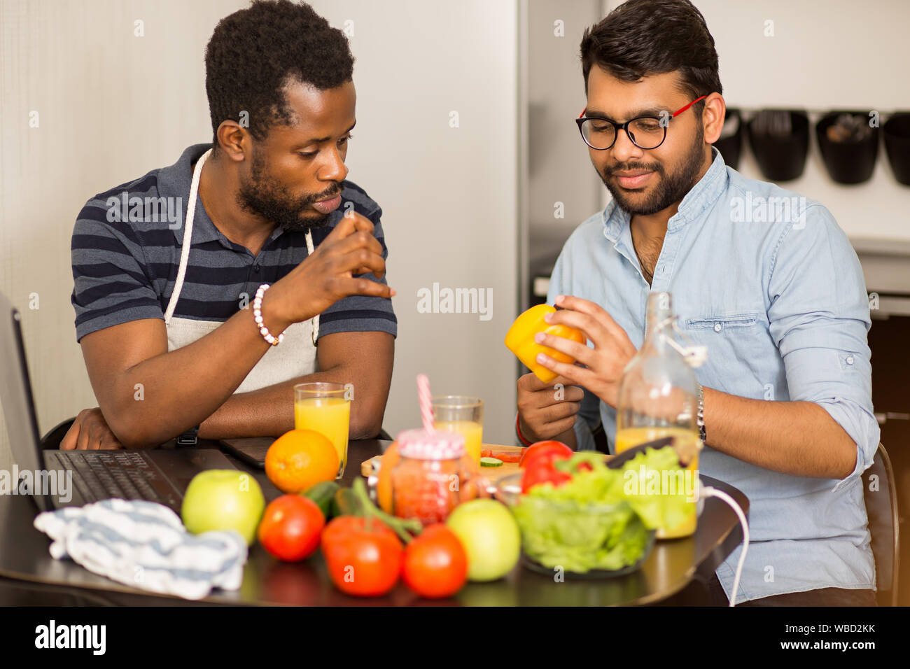 Two multi ethnic students sitting at table in kitchen watching a video ...
