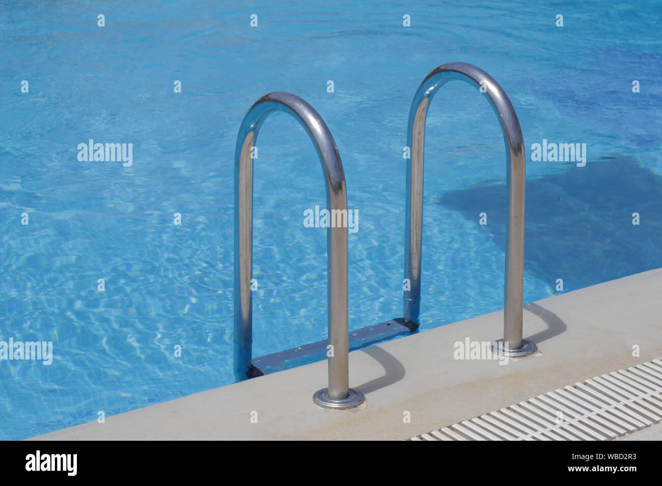 Ladder into the blue water in the pool. Blue pool rippled water. Azure ...