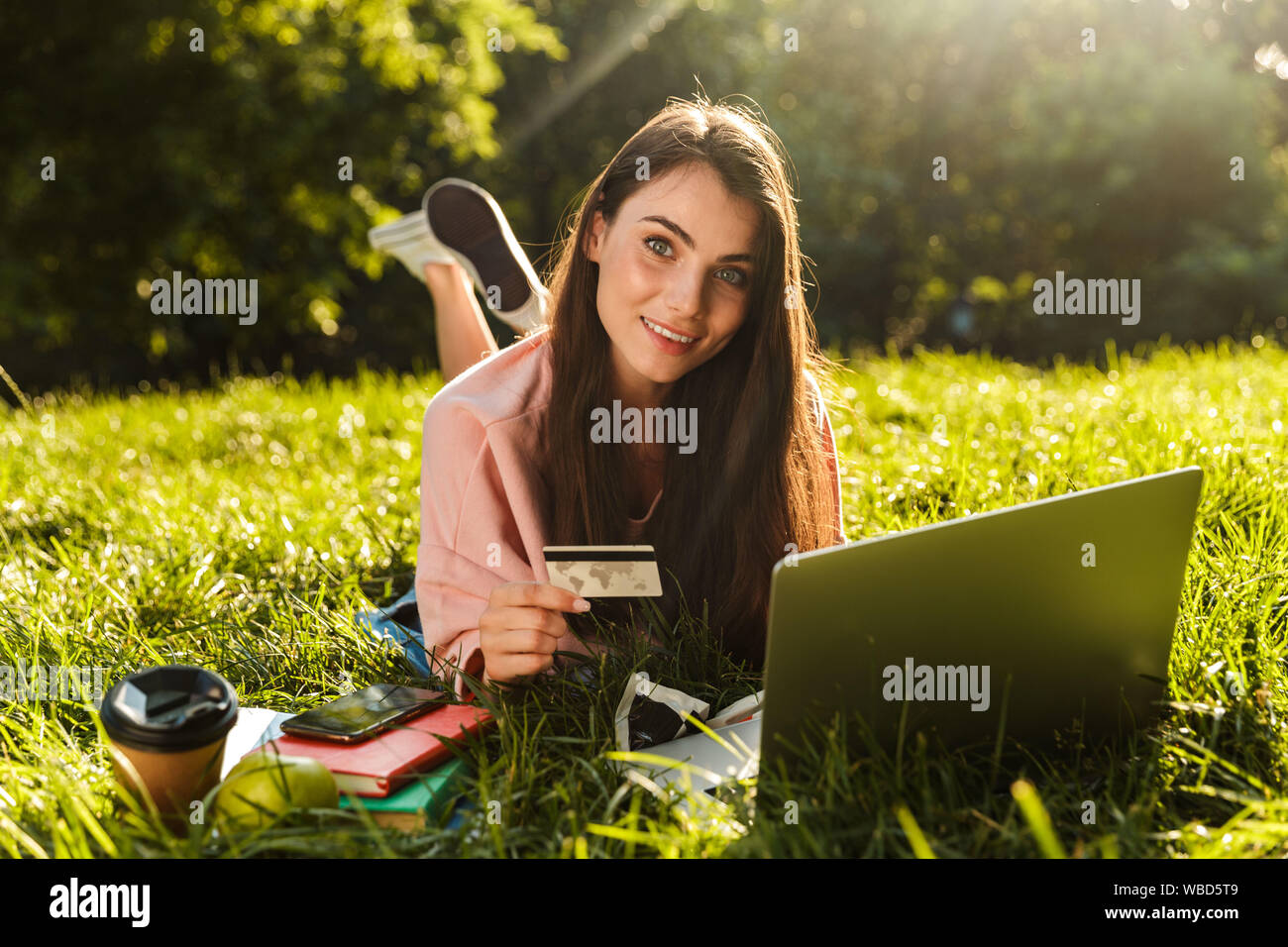 Pretty smiling young girl student studying on laptop computer while ...