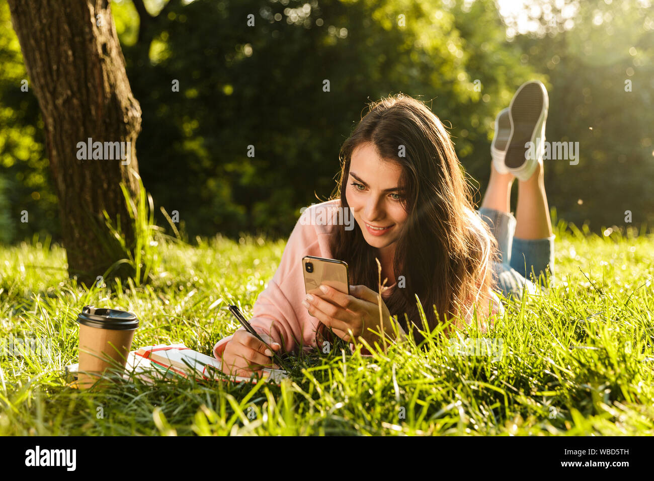 Pretty young girl student using mobile phone while laying on a grass at ...