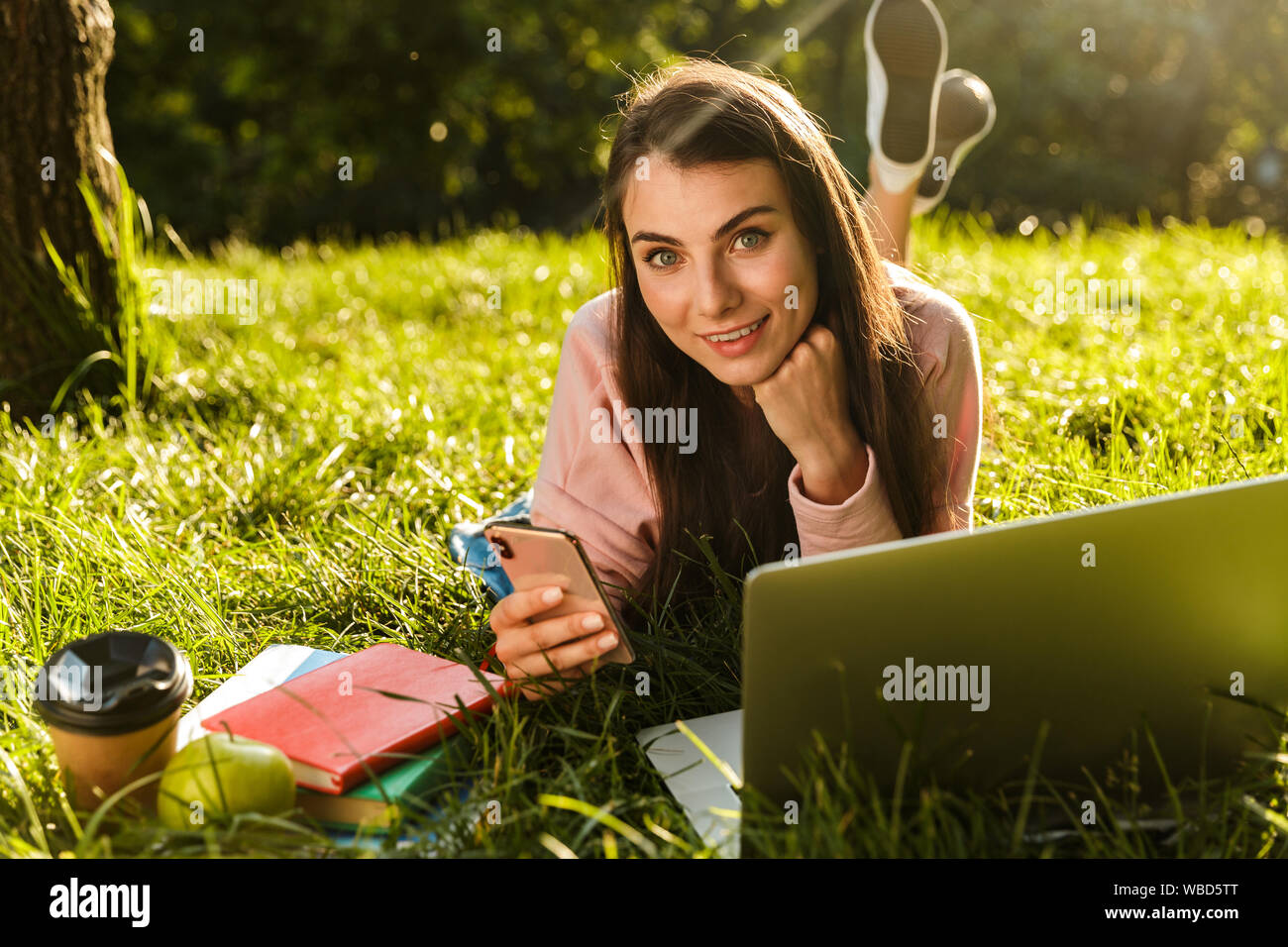 Pretty smiling young girl student studying on laptop computer while ...