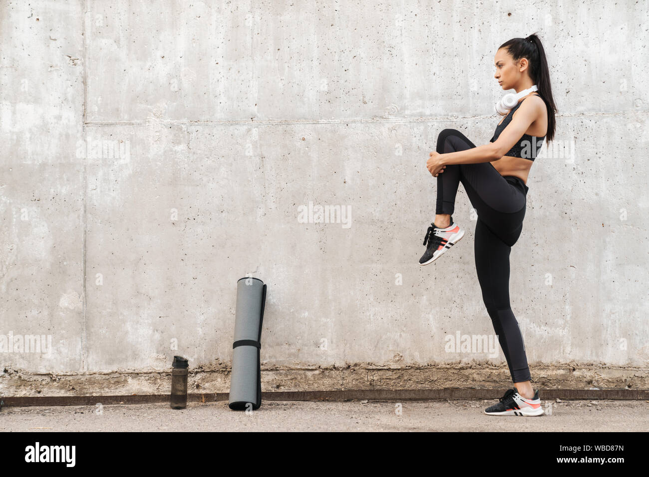Side view of an attractive young fitness girl standing outdoors, doing ...