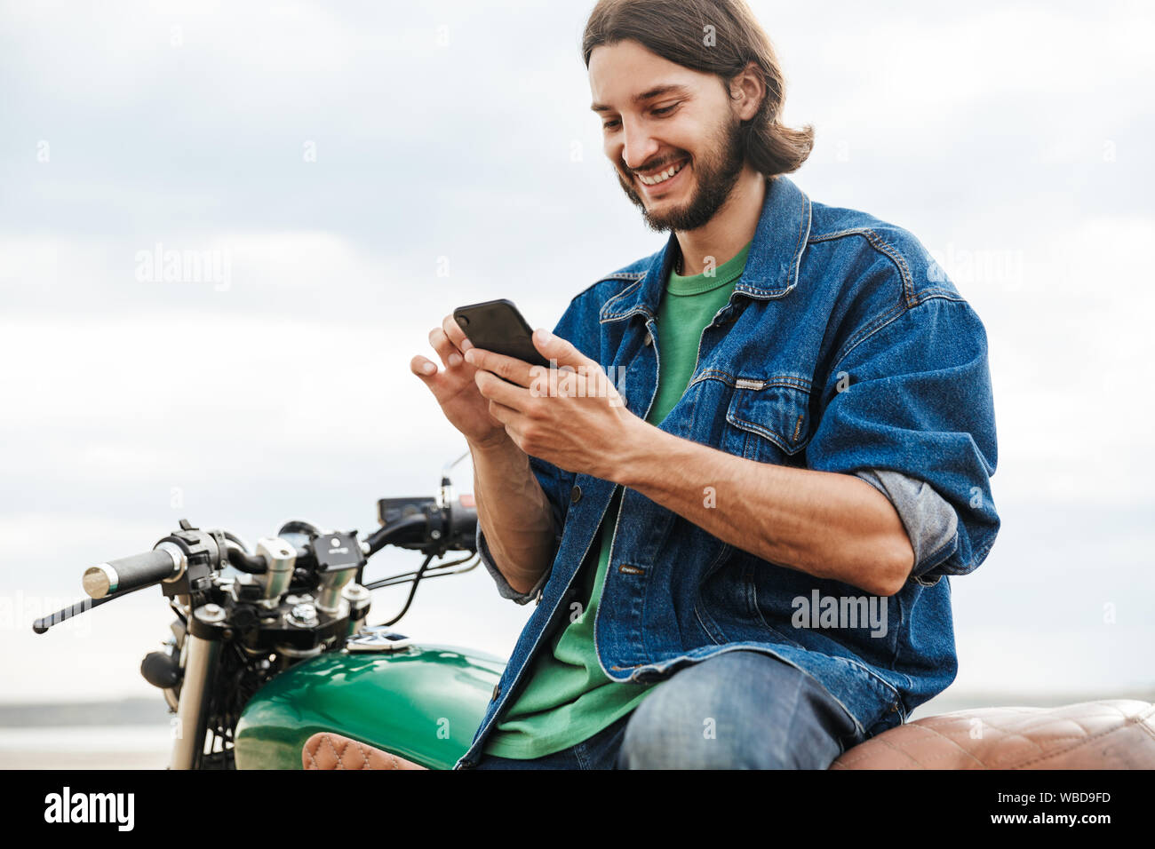 Picture of a cheery pleased man biker on his bike outdoors on a beach ...