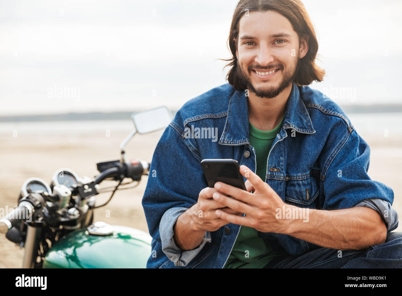 Picture of a cheery pleased man biker on his bike outdoors on a beach ...