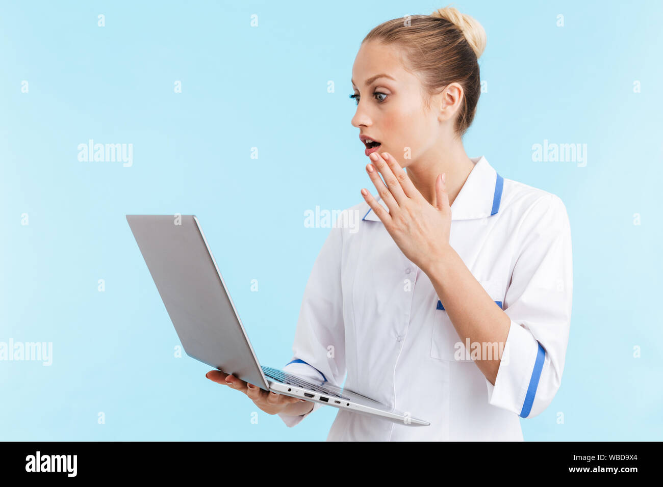 Beautiful shocked blonde woman doctor wearing uniform standing isolated ...