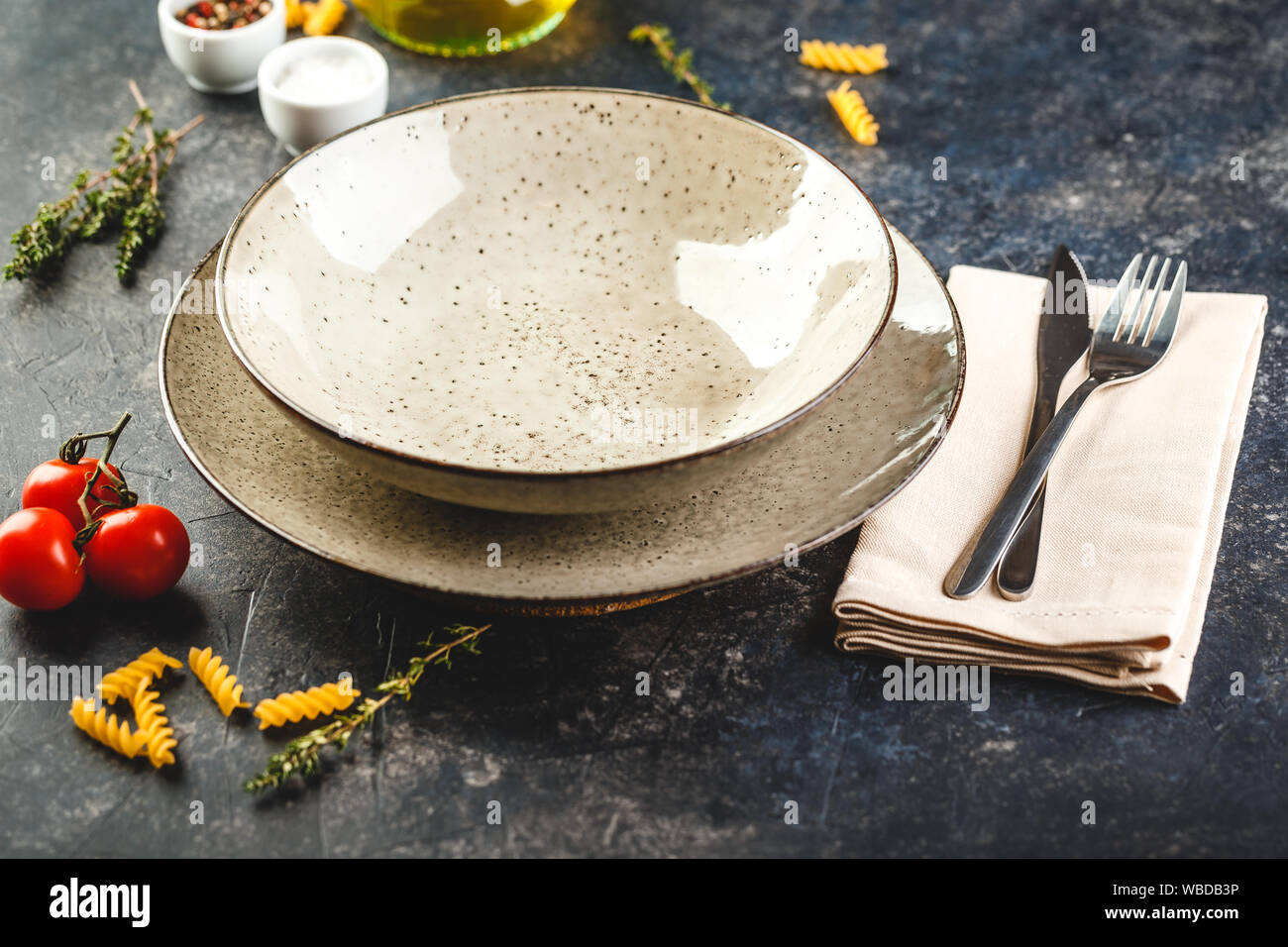 Table setting with cutlery, pasta Fusilli, tomatoes and herbs on dark ...