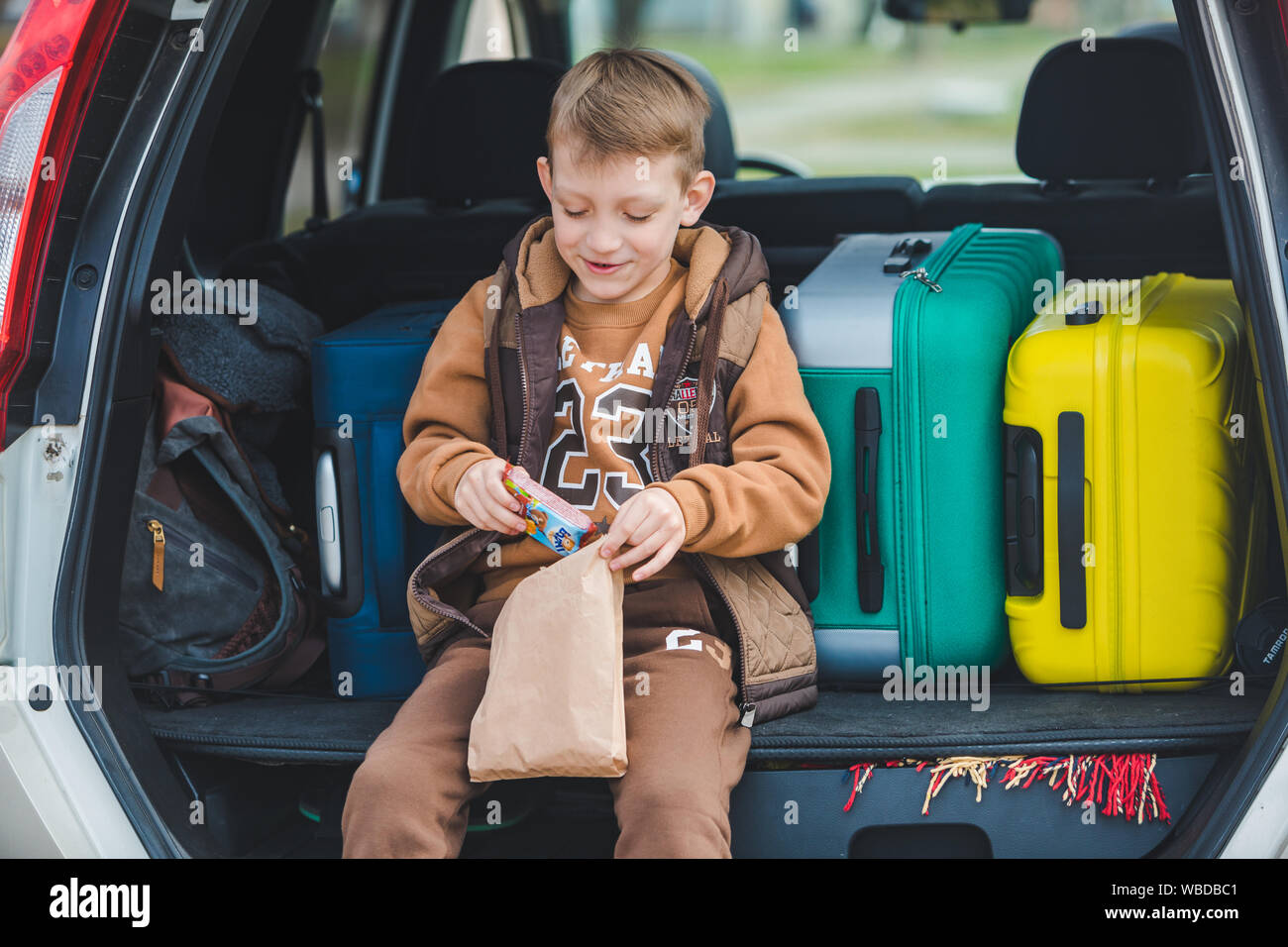 little kid looking into paper bag with candies sitting in car trunk ...