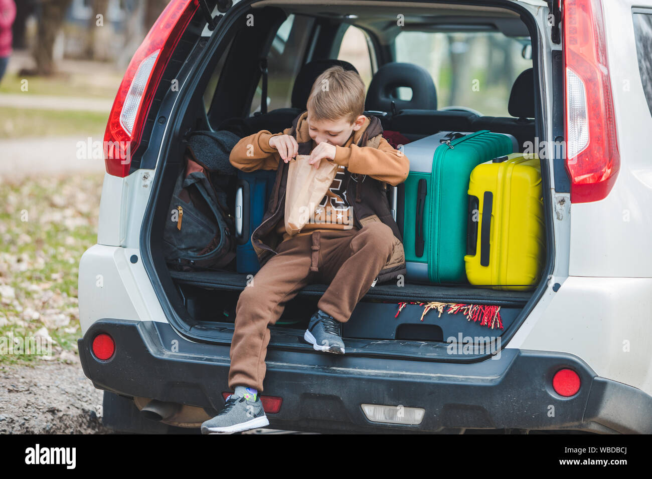 little kid looking into paper bag with candies sitting in car trunk ...