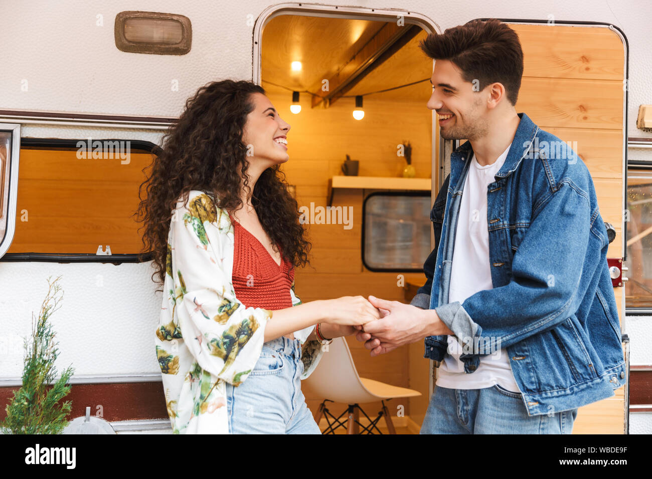 Cheerful young couple talking while standing at the campvan, holding ...