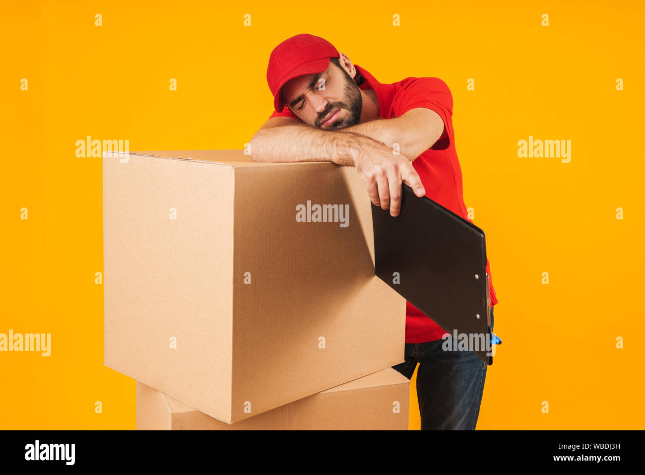 Image of young delivery man in red uniform sleeping while standing with ...