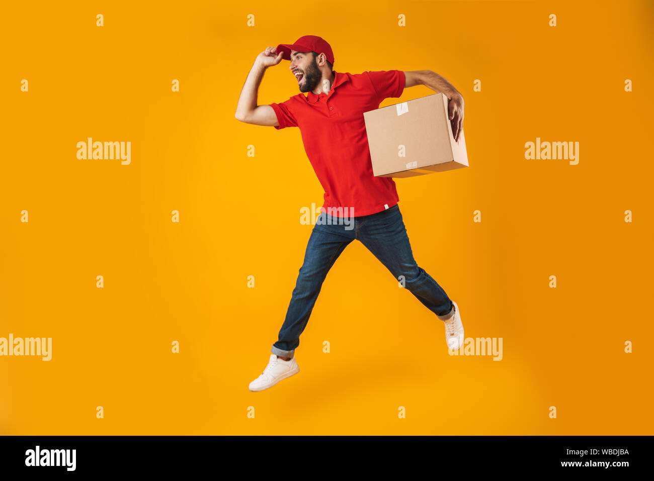 Portrait of excited delivery man in red uniform running and holding ...