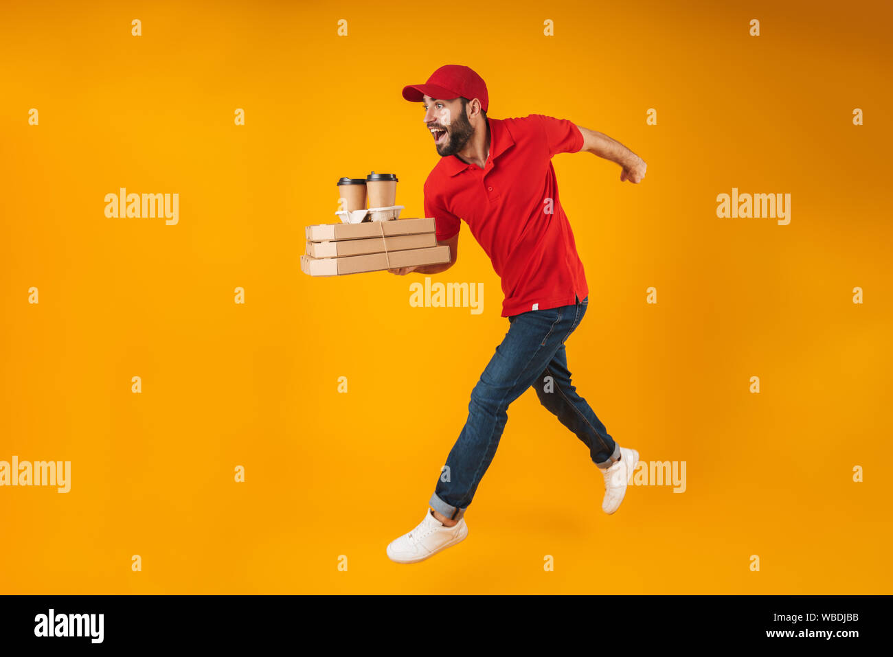 Portrait of young delivery man in red uniform running with pizza boxes ...