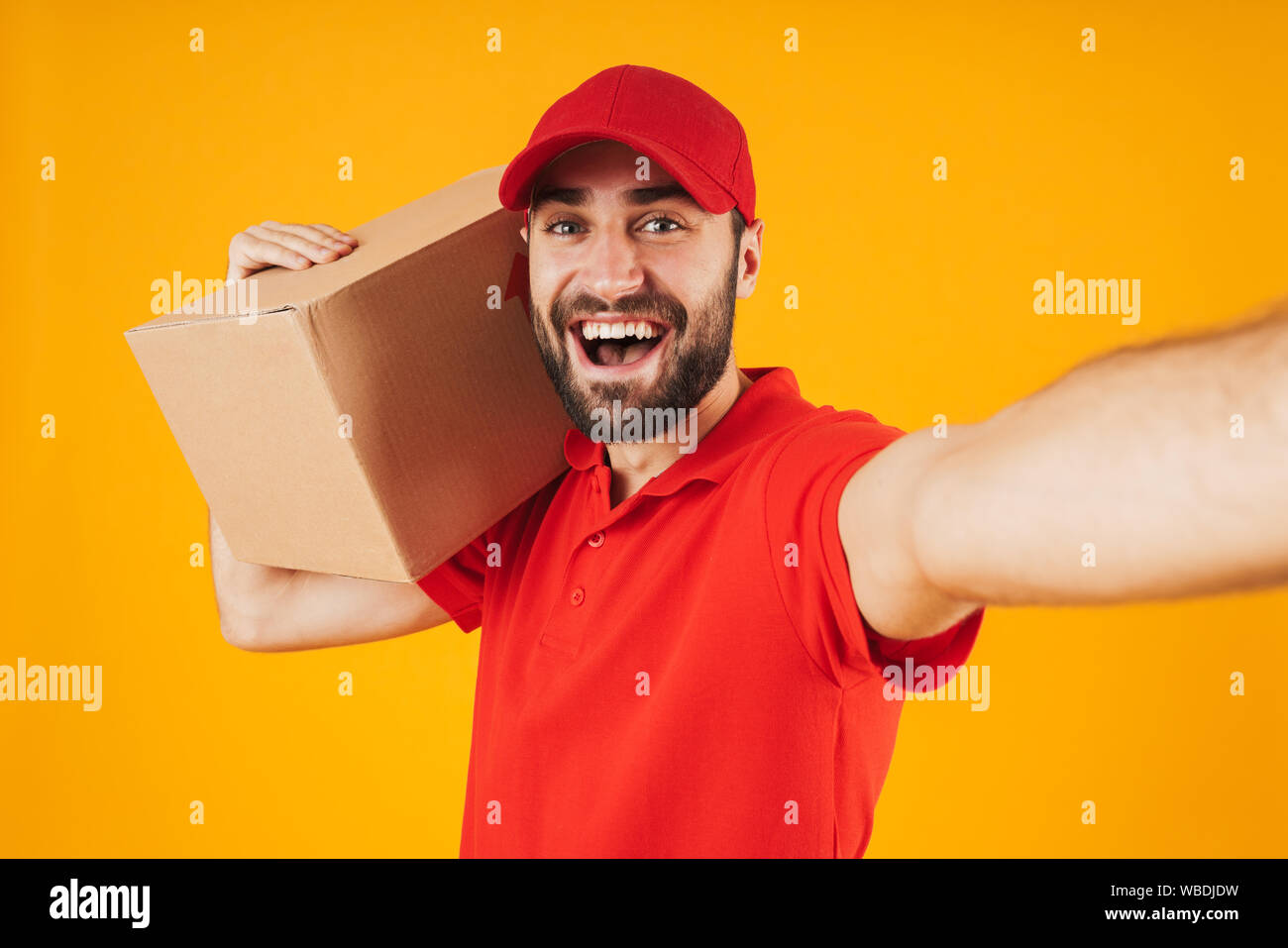 Portrait of handsome delivery man in red uniform smiling and holding ...