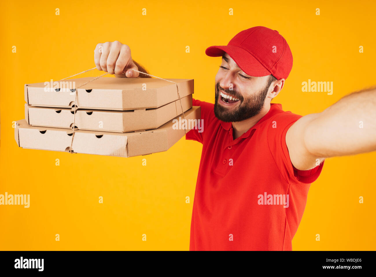 Portrait of positive delivery man in red uniform smiling and holding ...