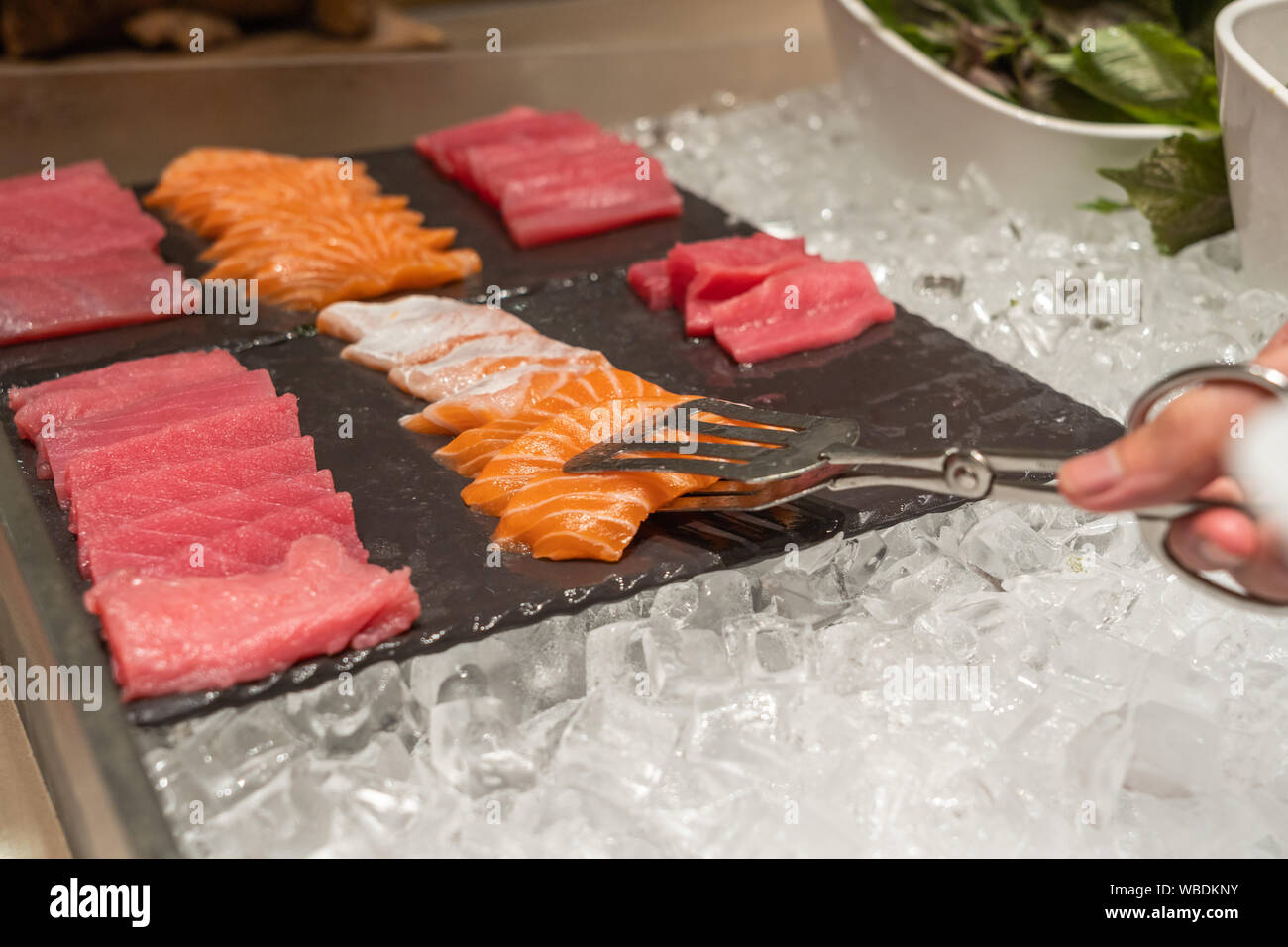 Human hand using tongs picking sashimi in sushi buffet meal Stock Photo ...