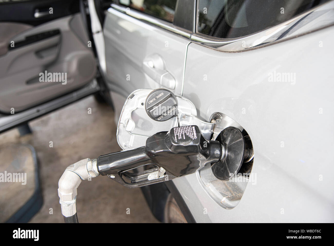 A silver-color vehicle’s empty gas tank is being filled with fuel at ...