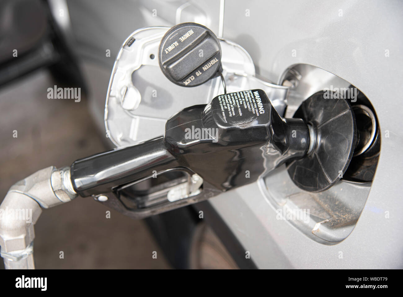 A silver-color vehicle’s empty gas tank is being filled with fuel at ...