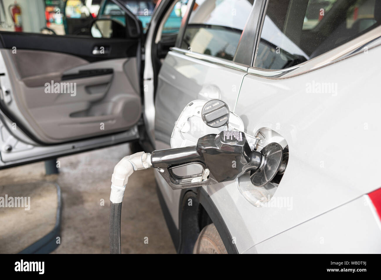 A silver-color vehicle’s empty gas tank is being filled with fuel at ...