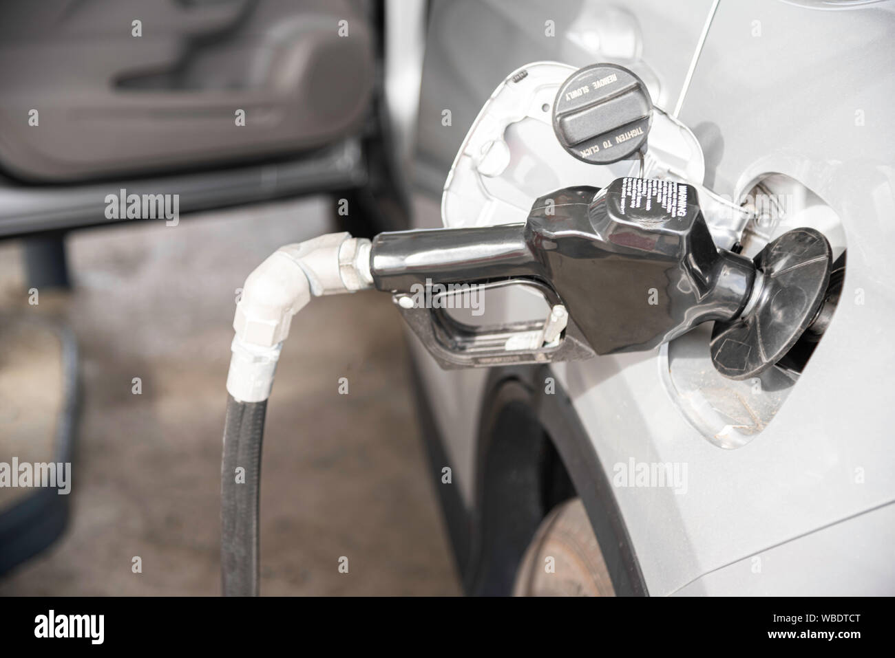 A silver-color vehicle’s empty gas tank is being filled with fuel at ...