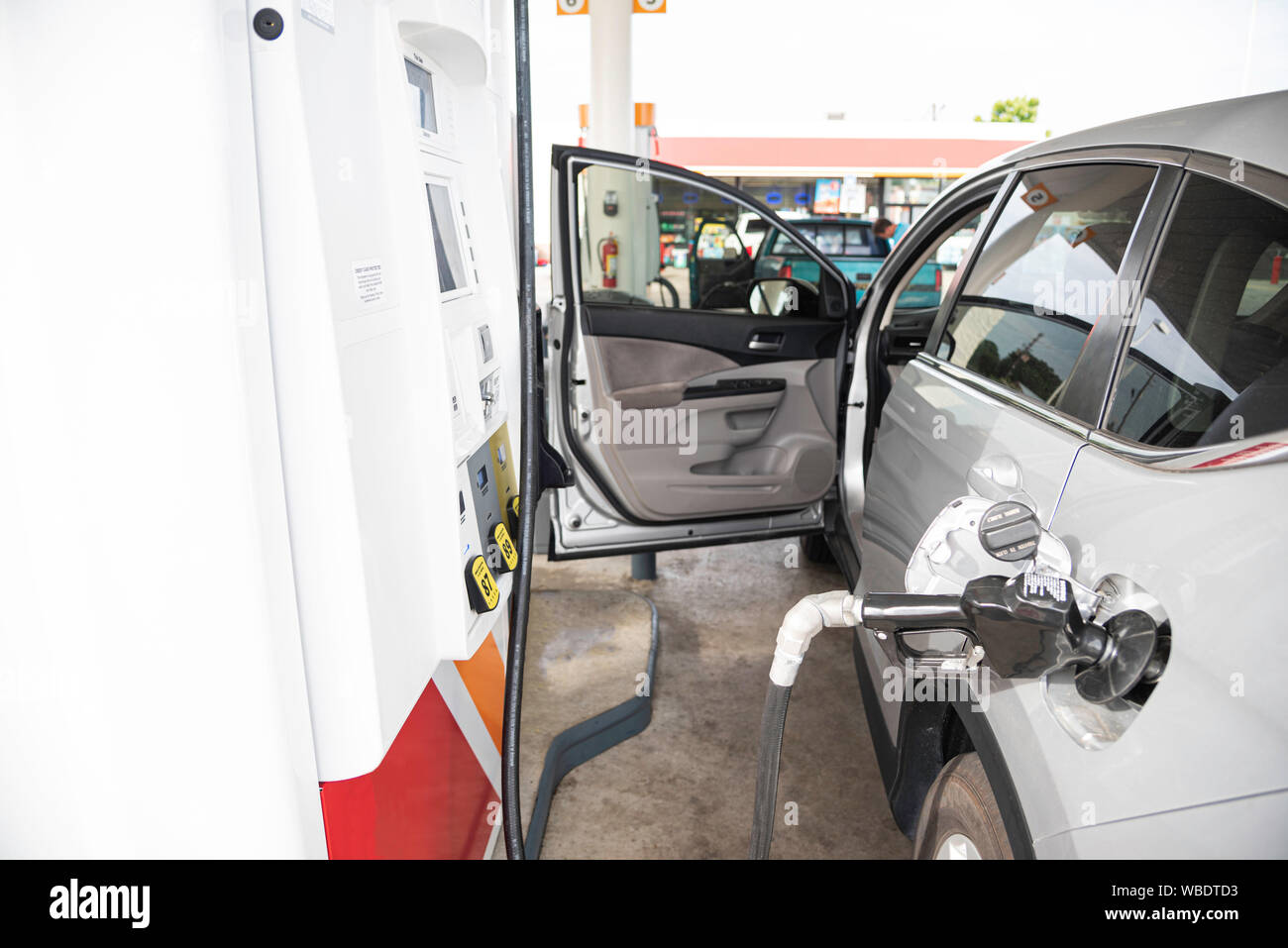 A silver-color vehicle’s empty gas tank is being filled with fuel at ...