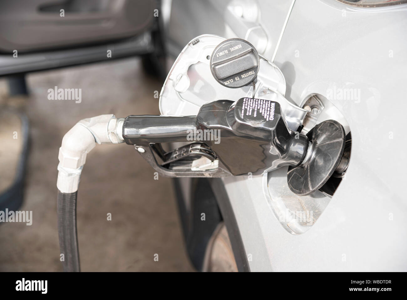 A silver-color vehicle’s empty gas tank is being filled with fuel at ...