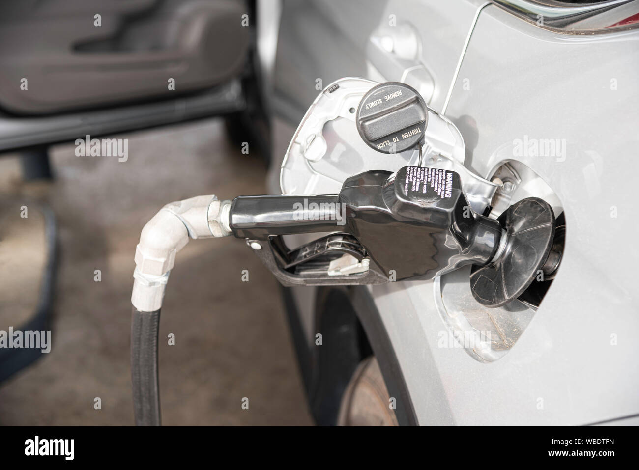 A silver-color vehicle’s empty gas tank is being filled with fuel at ...