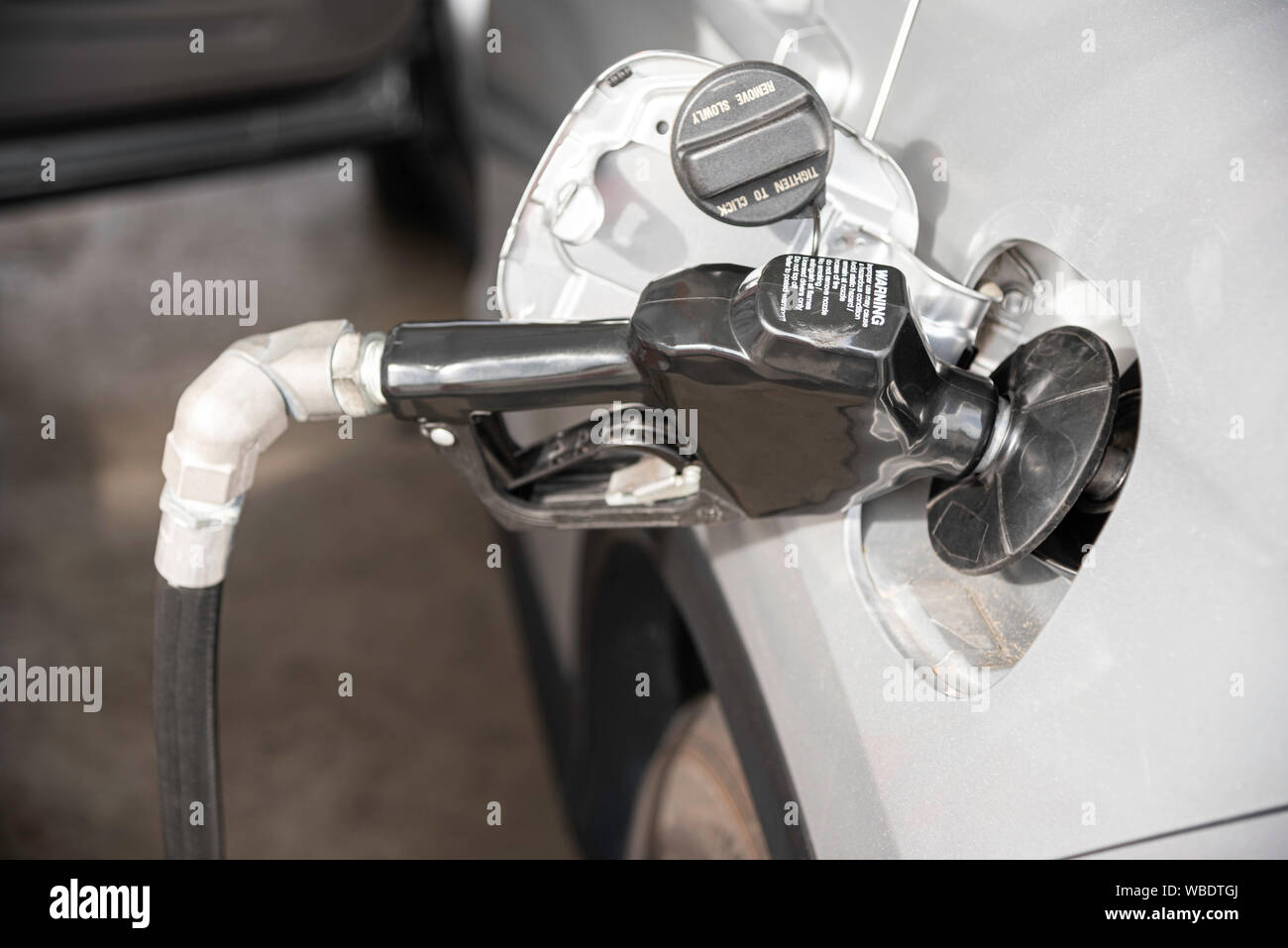 A silver-color vehicle’s empty gas tank is being filled with fuel at ...