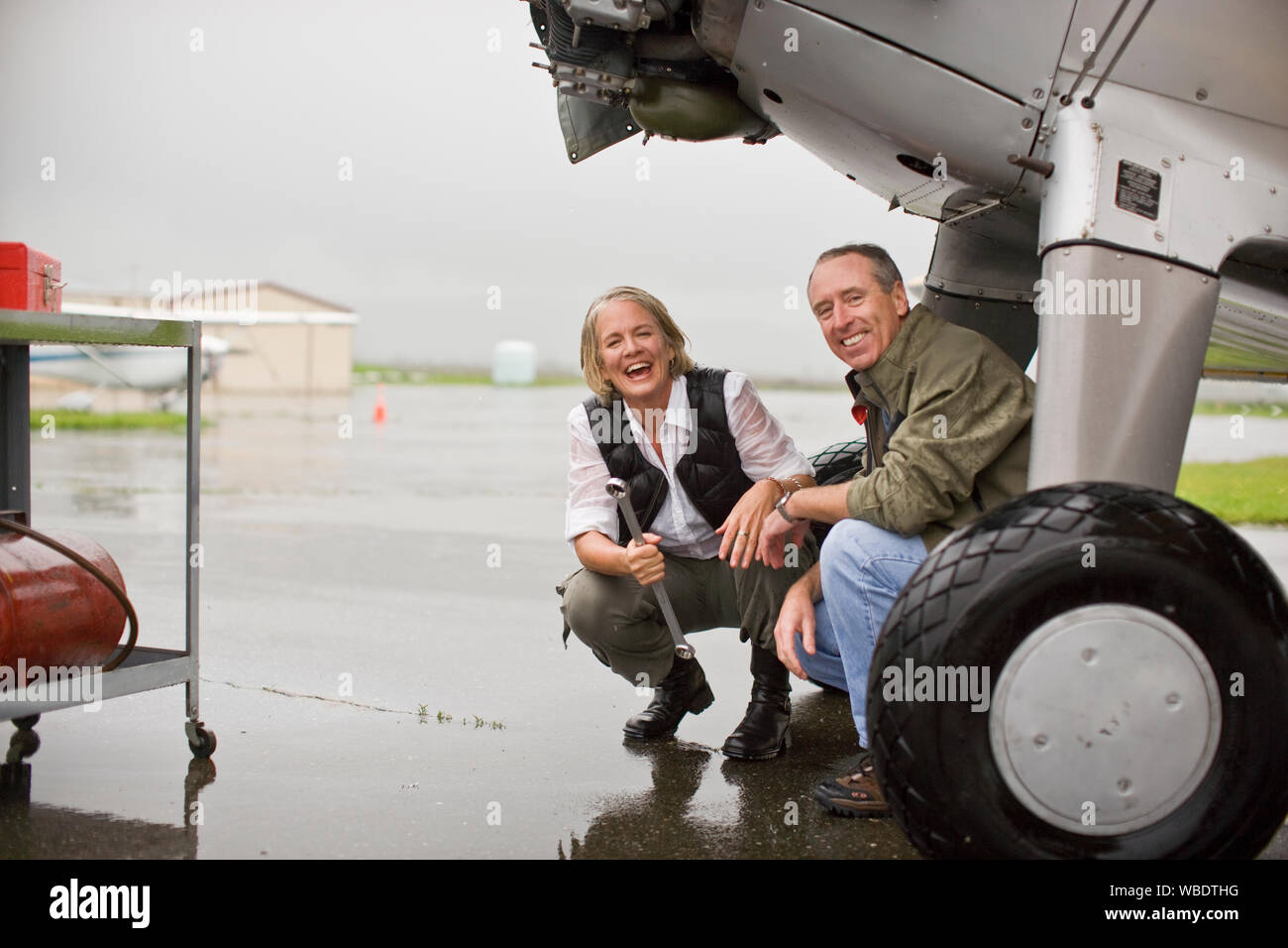 Man and woman crouching under airplane while it rains Stock Photo - Alamy