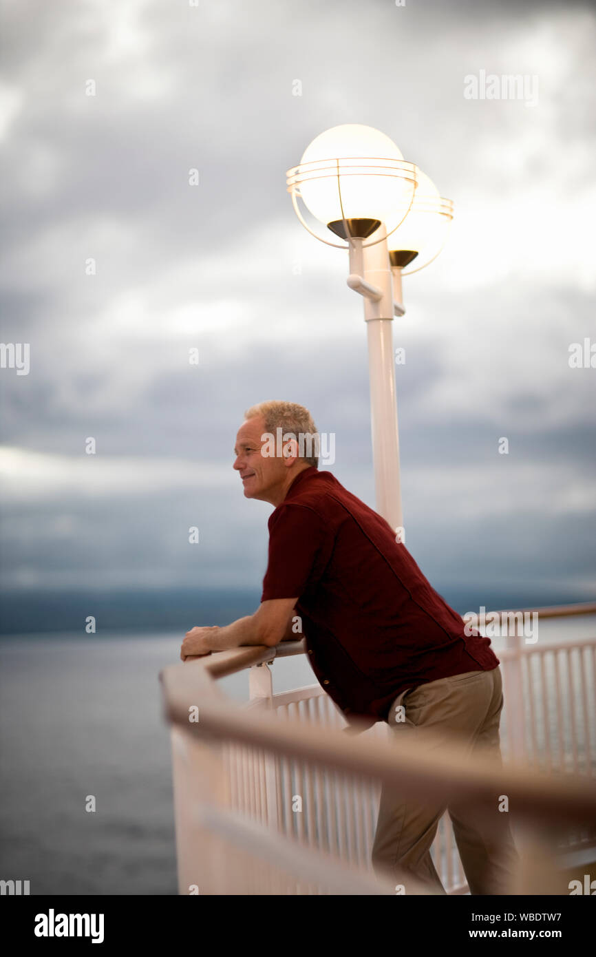 Mature man happily leans on a railing and gazes out at the view from a ...