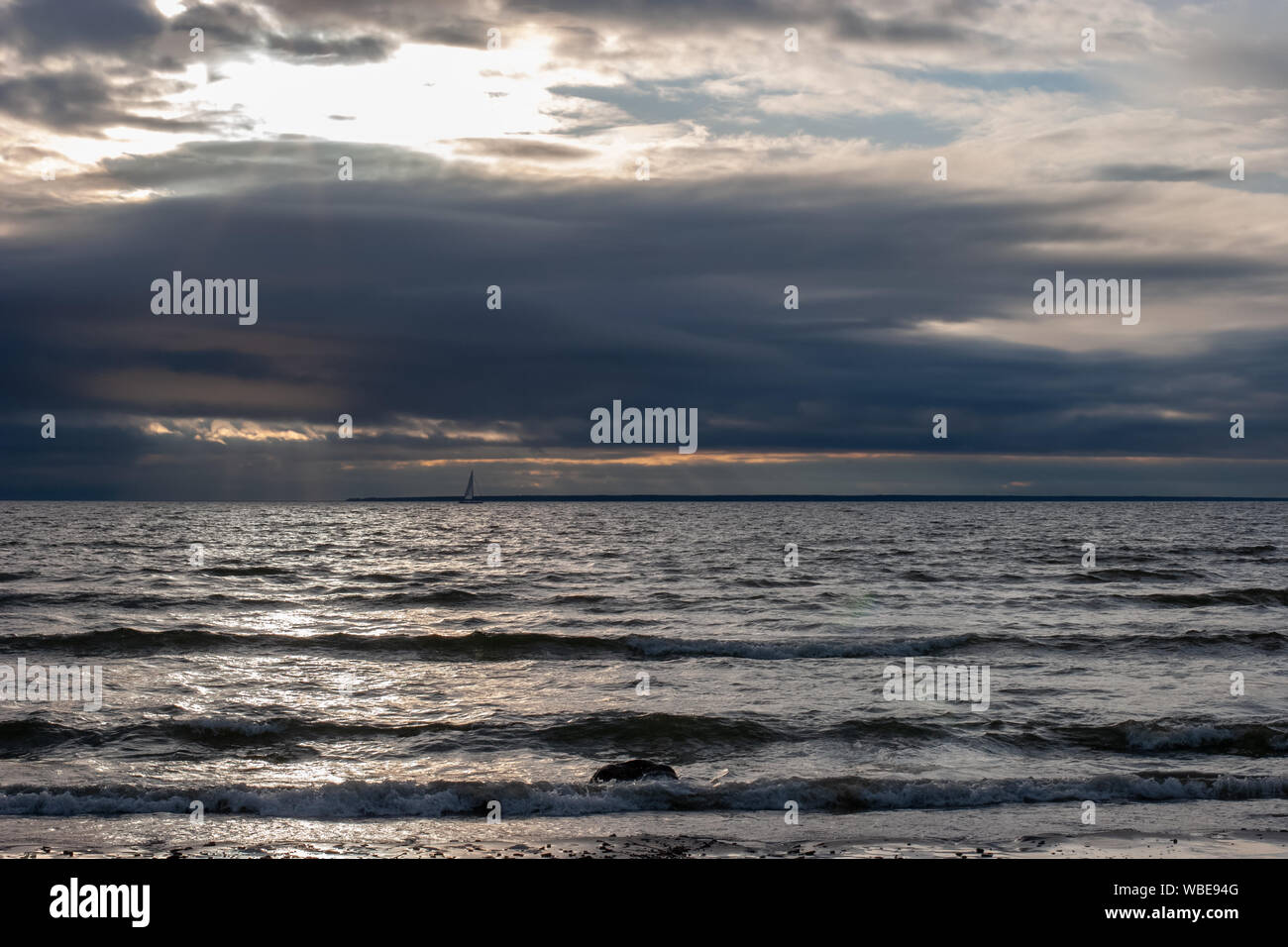 Bad weather sea with a boat with a sail on the horizon. The sun through ...