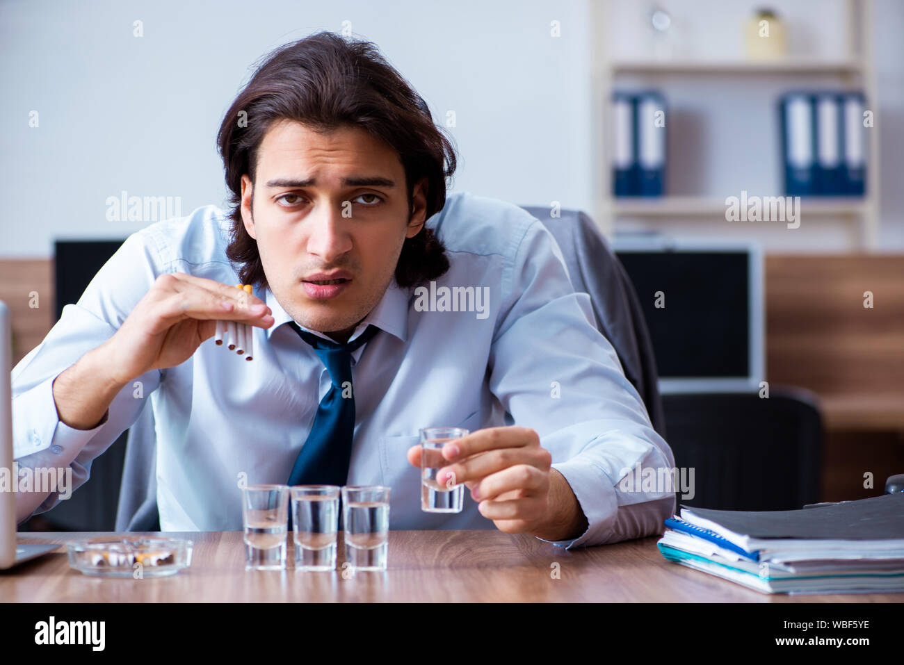 The male employee drinking vodka and smoking cigarettes at workplace ...